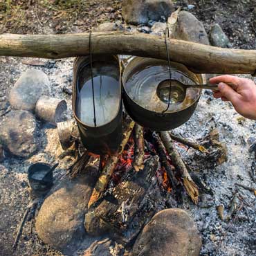 man ladling boiling water over a campfire | Against Global Hunger